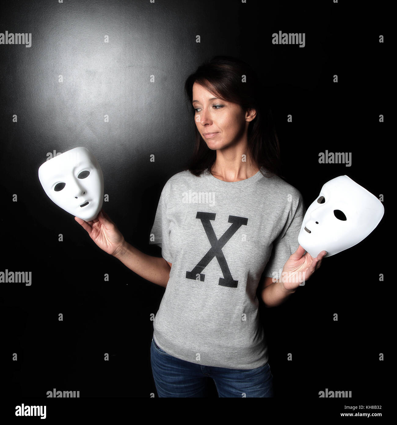 Brown woman in a studio wearing a T-shirt with an X and holding a mask ...