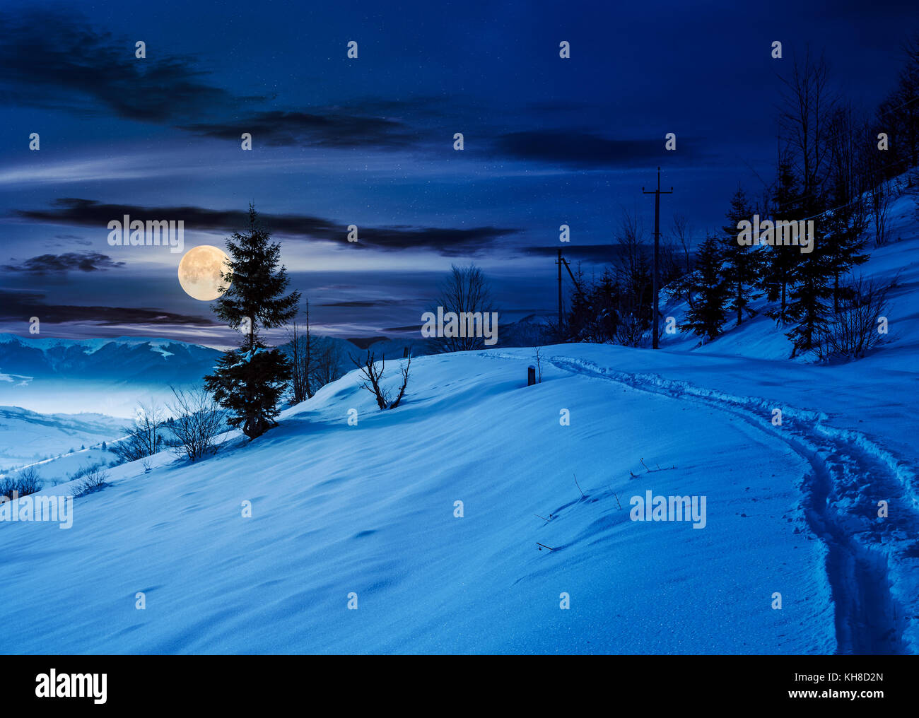rural footpath through snowy hillside at night in full moon light ...