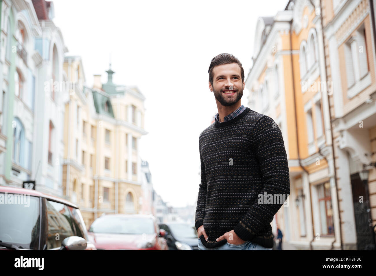 Portrait of a happy bearded man in sweater standing on a city street ...