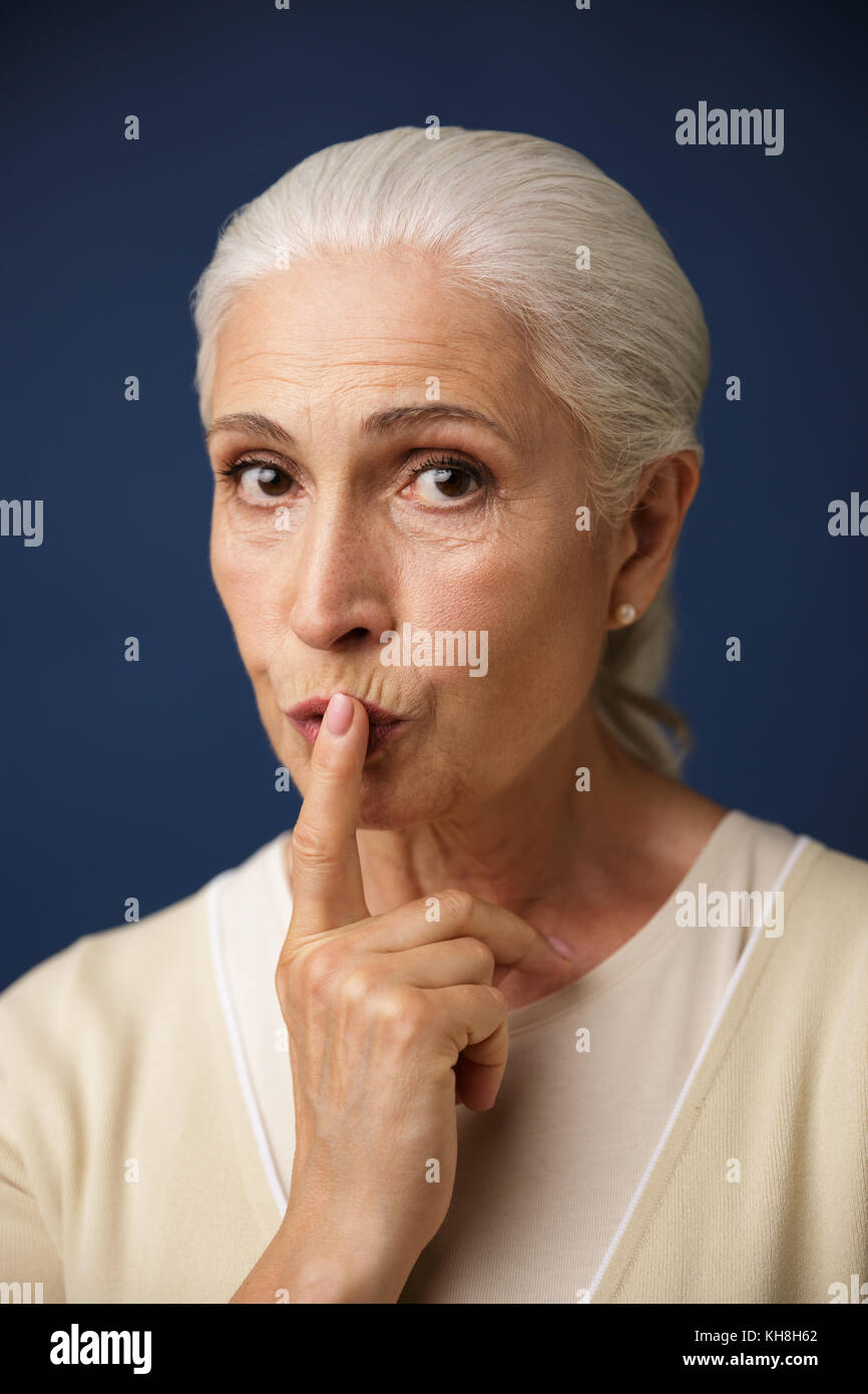 Close-up portrait of beautiful old woman, showing silence gesture, over ...