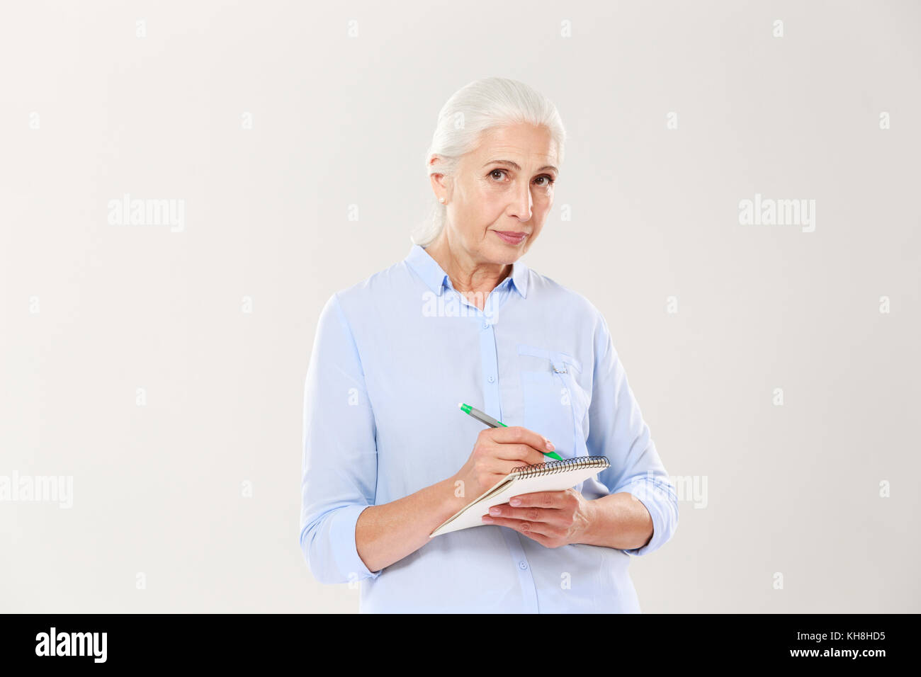 Confident serious mature woman in casual clothes writing in notebook ...
