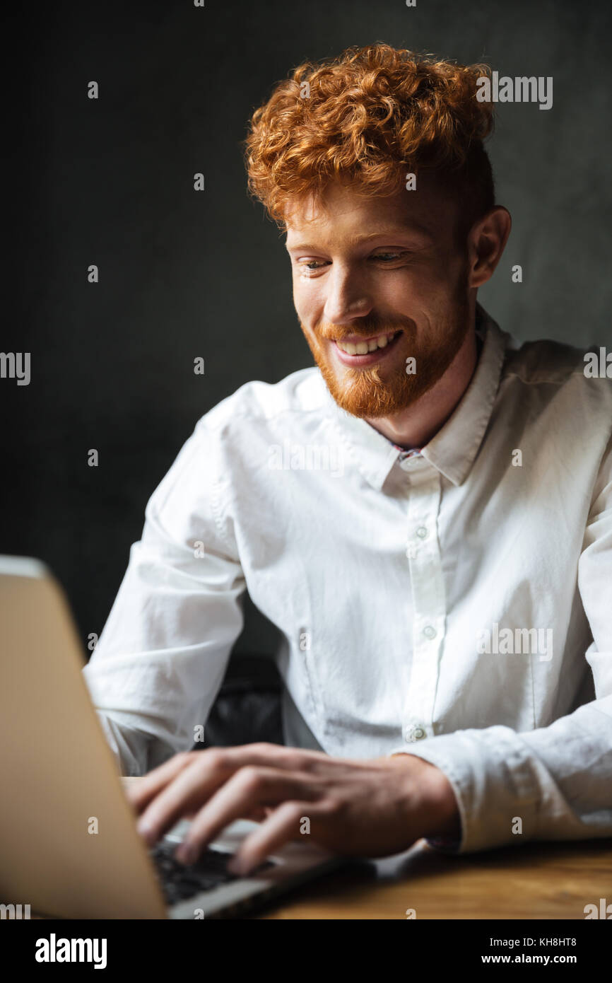 Portrait of a happy young man typing on a laptop while sitting at the ...