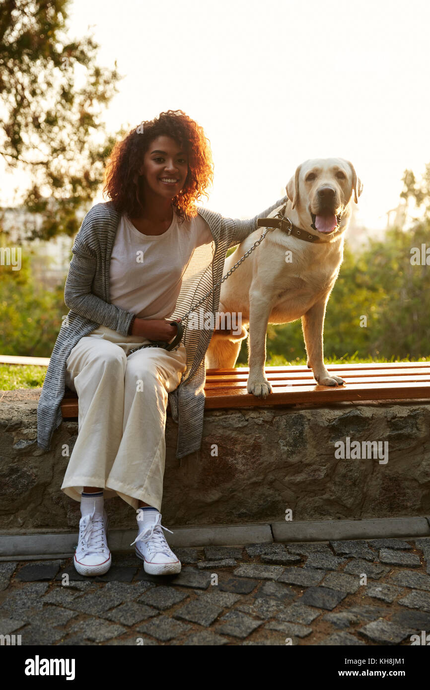 Young careless african lady sitting on bench in park and hugging her ...