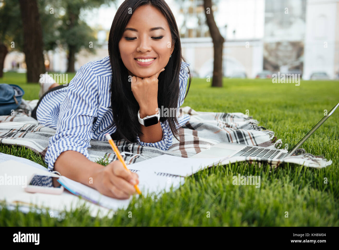 Pretty asian female student taking notes, lying on checkered plaid in ...