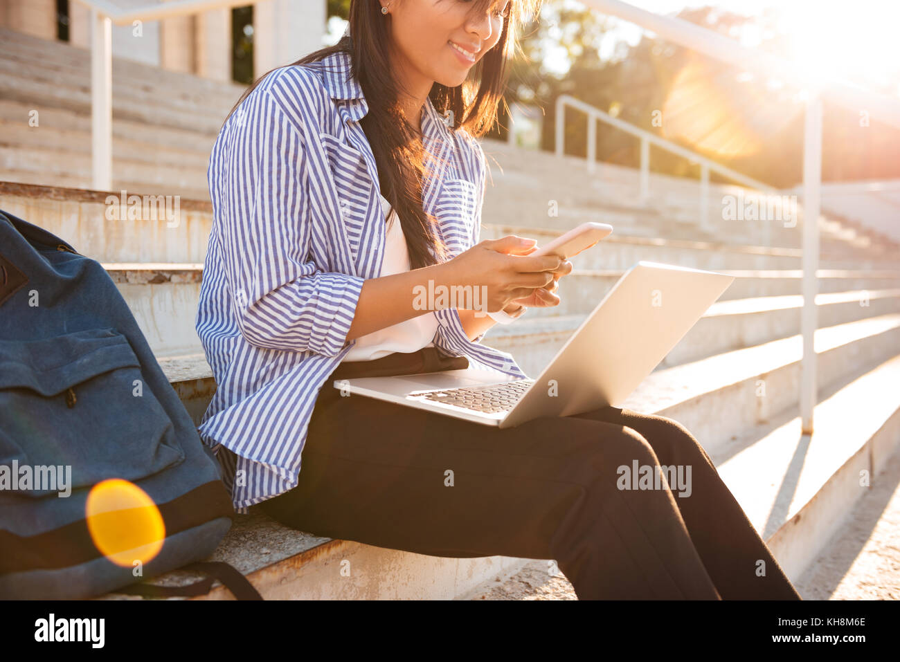 Photo of smiling asian female studen chatting on smartphone, while ...