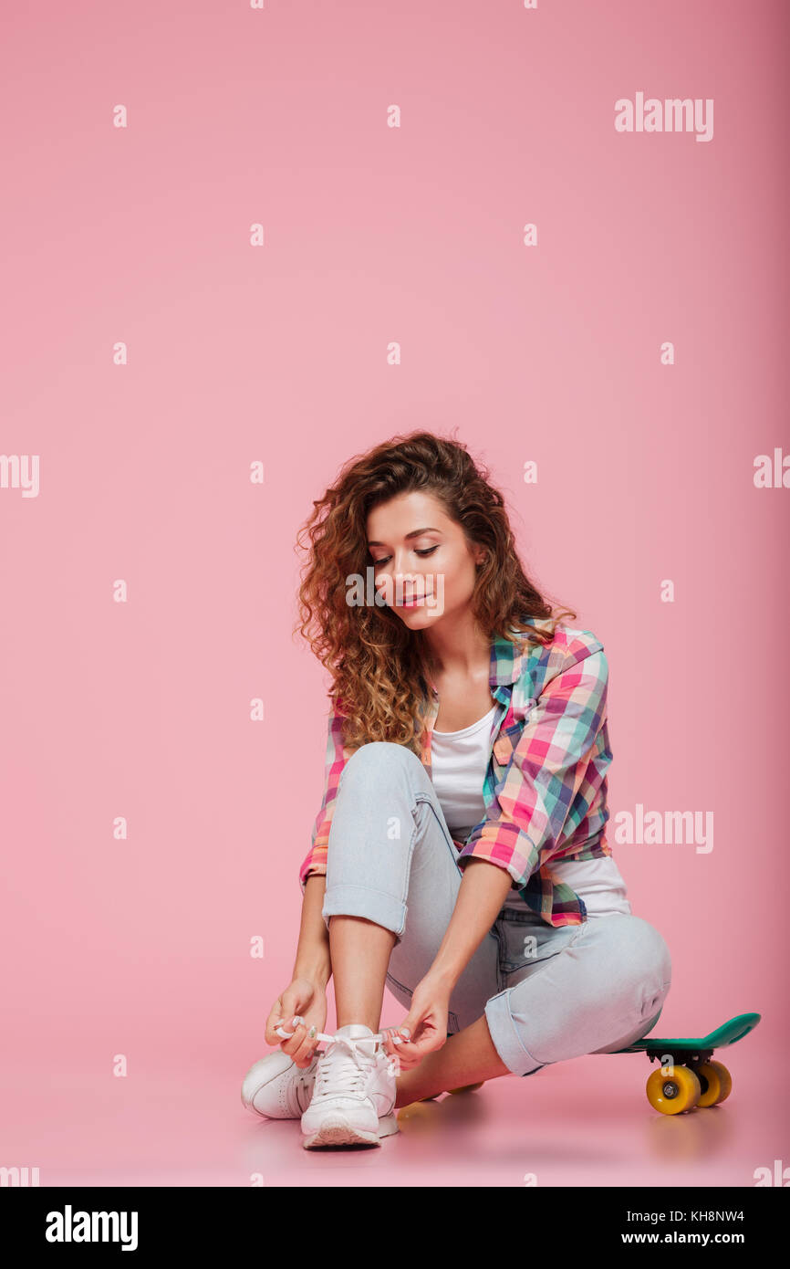 Young cute lady sitting on skateboard and tie shoelaces isolated over ...