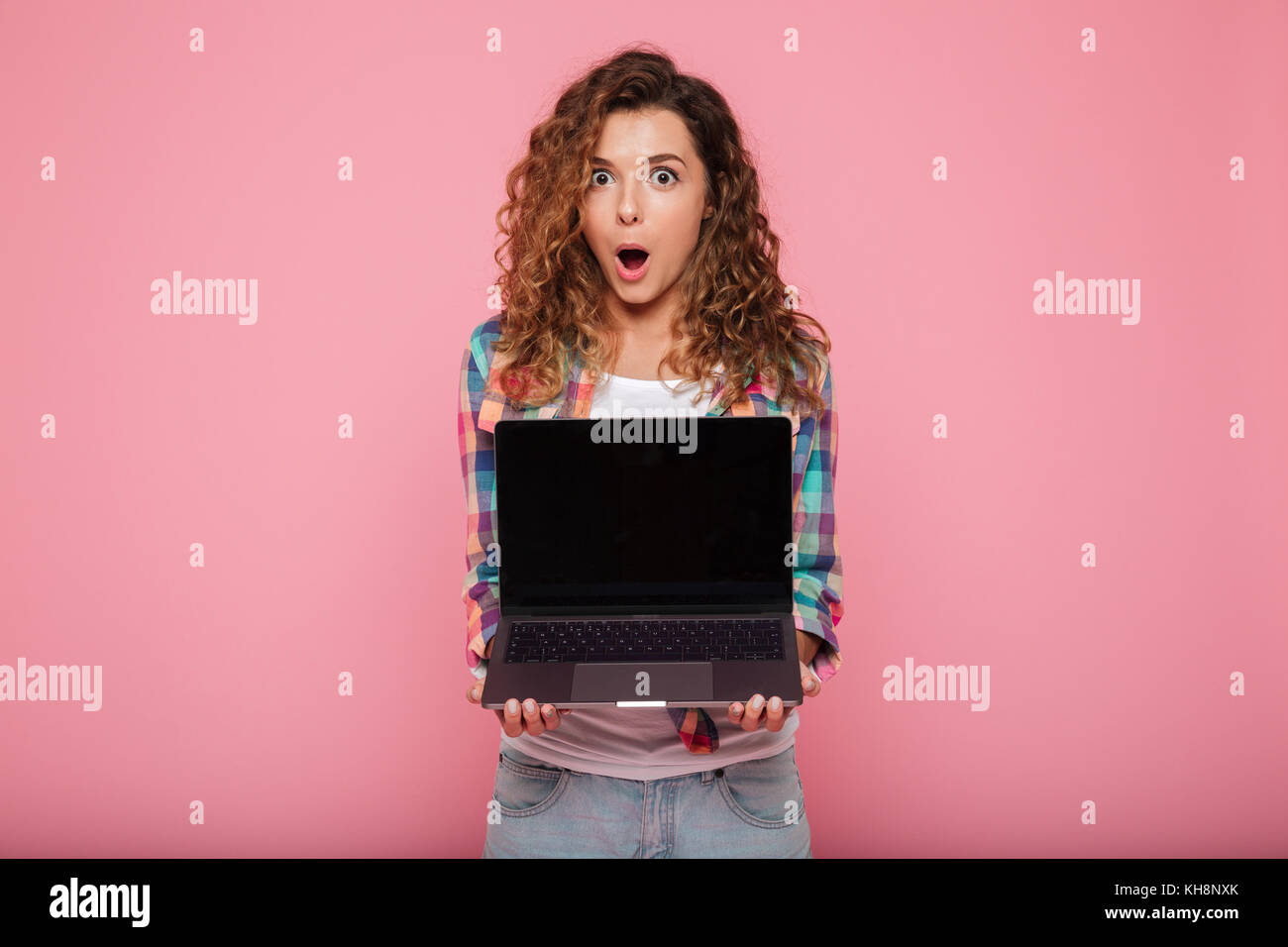 Surprised caucasian woman with curly hair showing laptop computer and ...