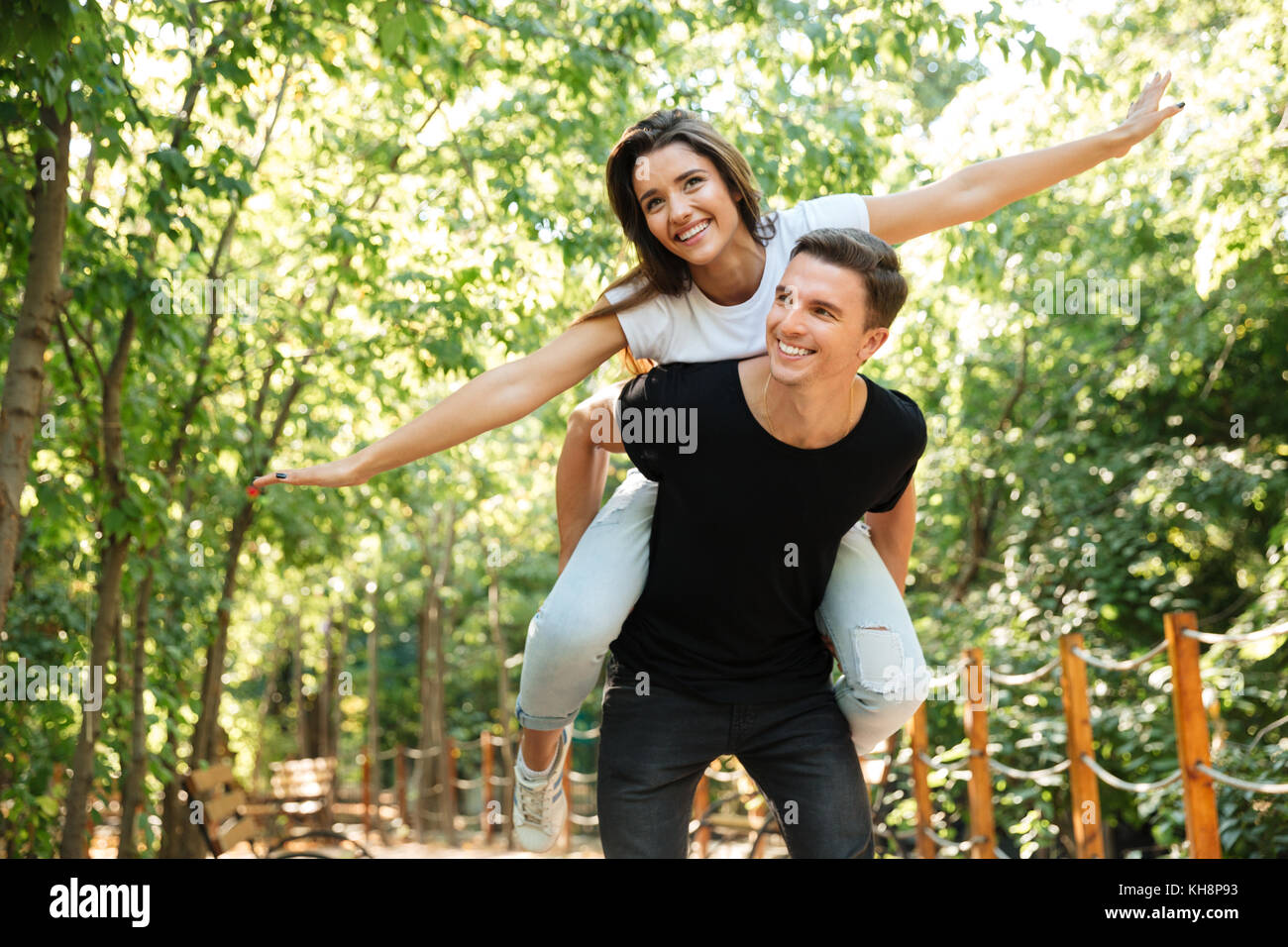 Young smiling couple enjoying piggyback ride and laughing at the park ...