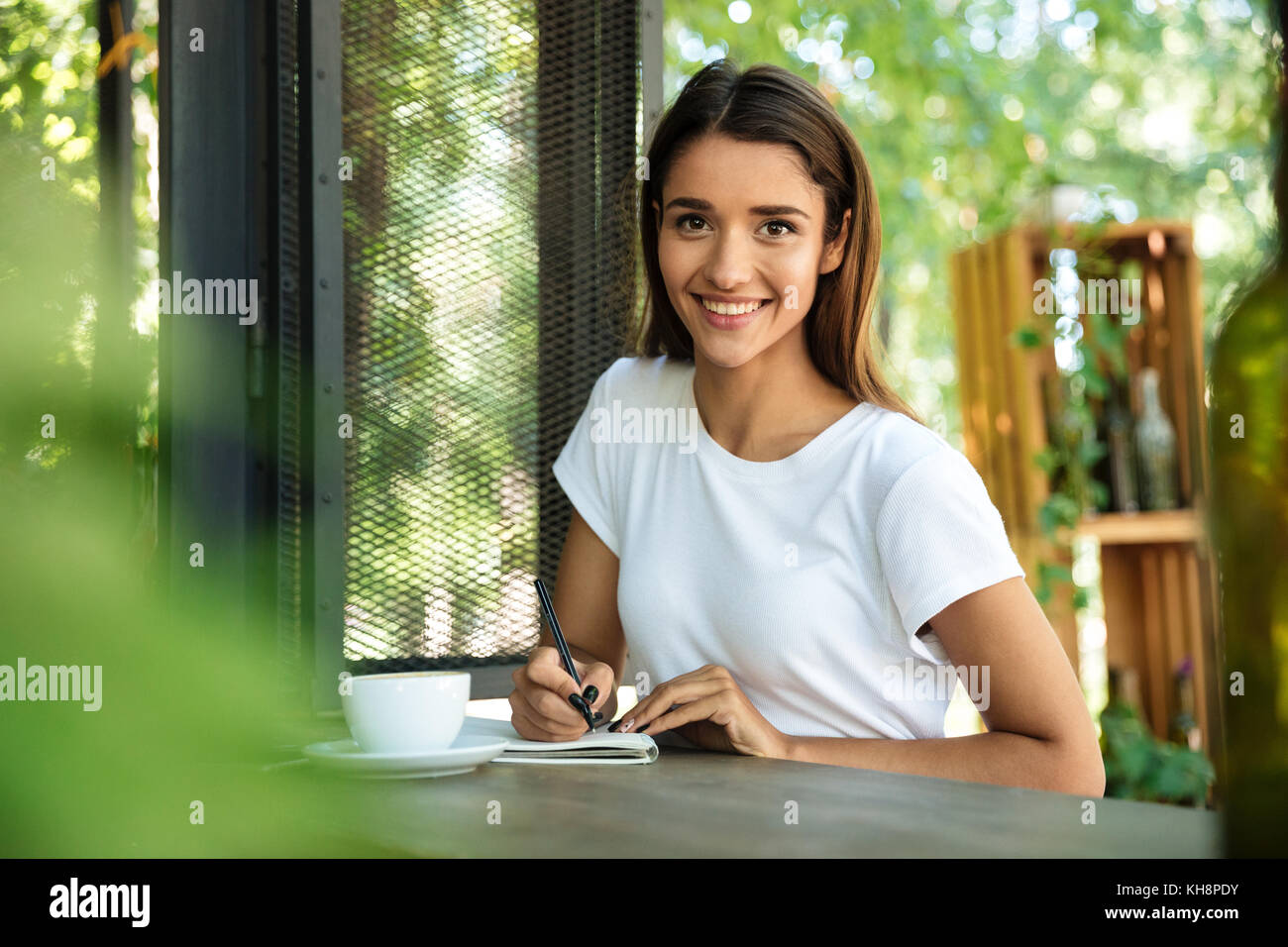 Portrait of a smiling beautiful girl making notes in a textbook while ...