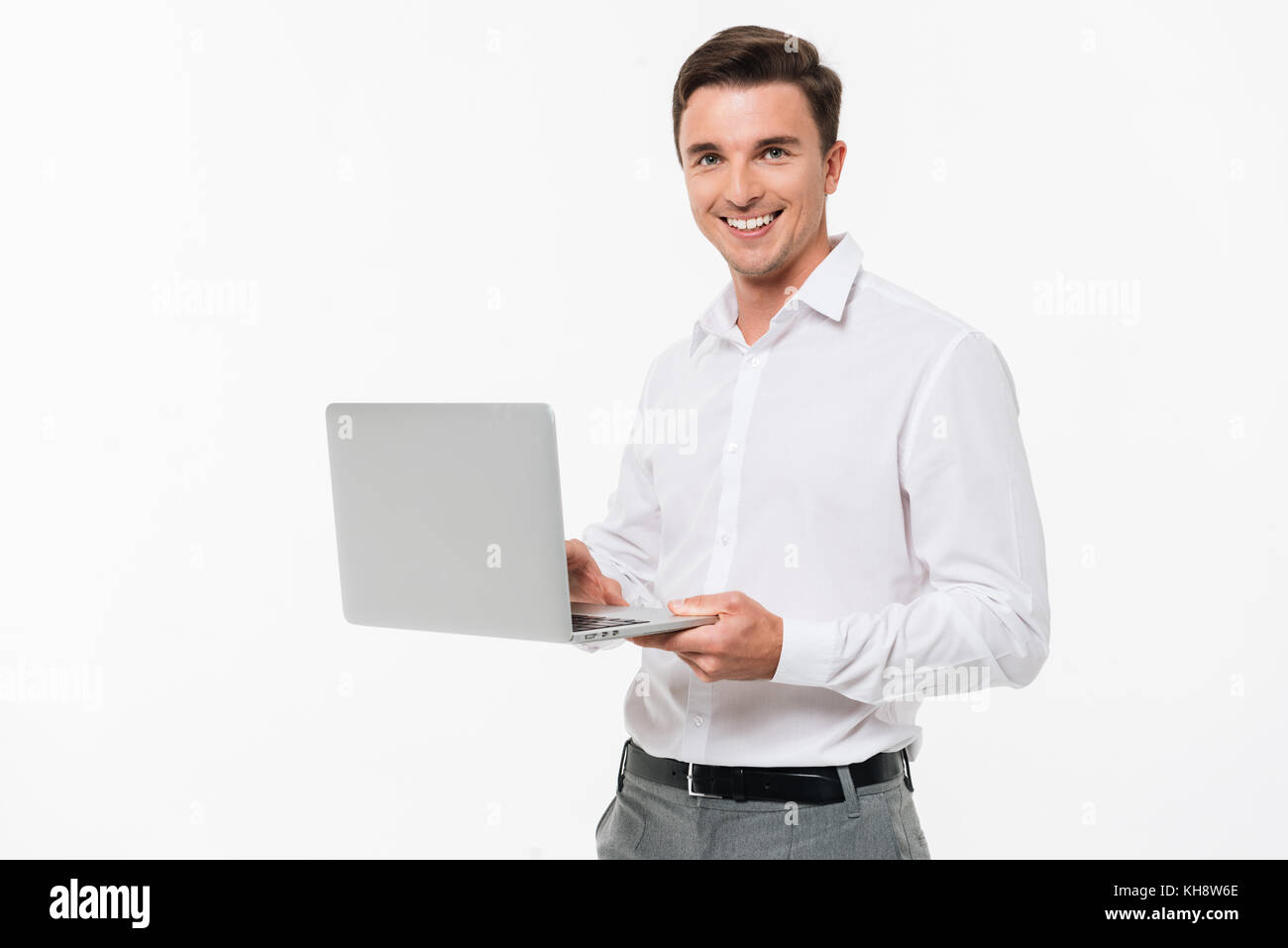 Portrait of a happy young man holding laptop computer while standing ...