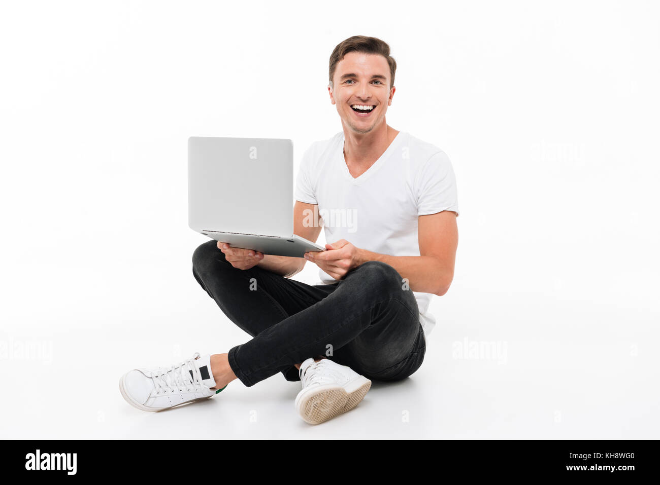 Portrait of an excited amused guy working on laptop computer while ...