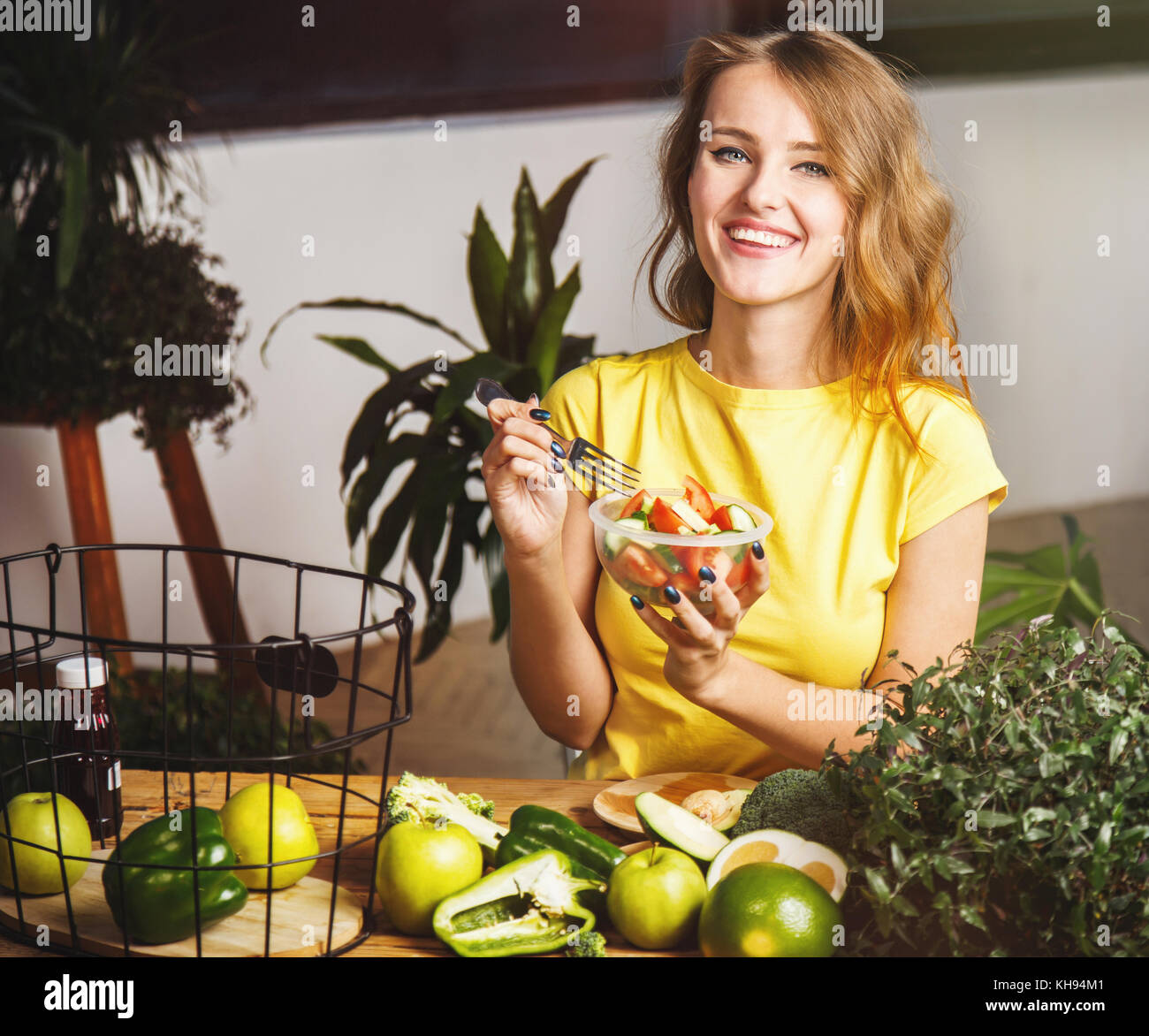 Attractive, slim girl eating vegetable salad at the wooden table full ...