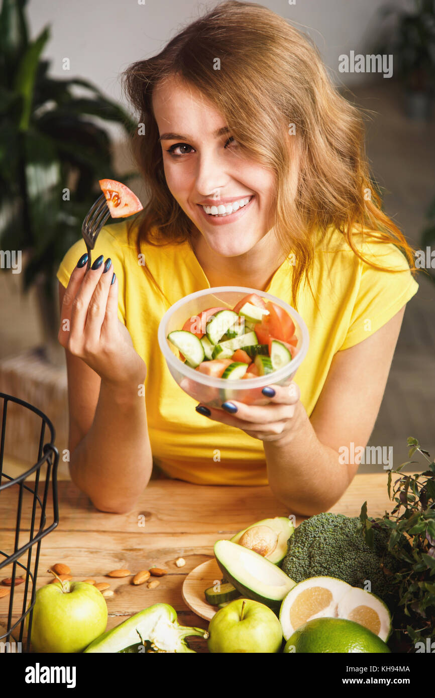 Attractive, slim girl eating vegetable salad at the wooden table full ...