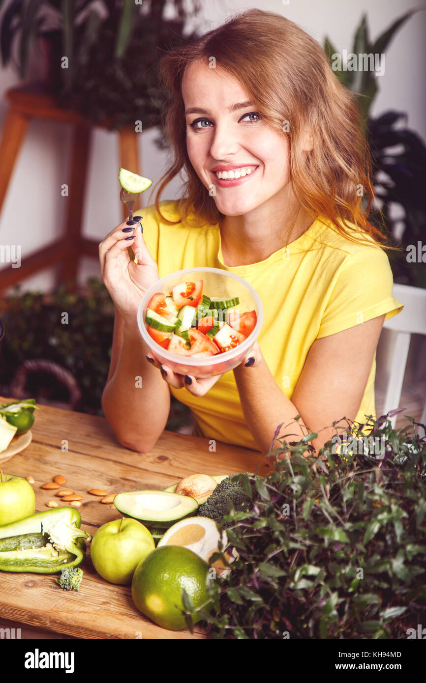 Attractive, slim girl eating vegetable salad at the wooden table full ...