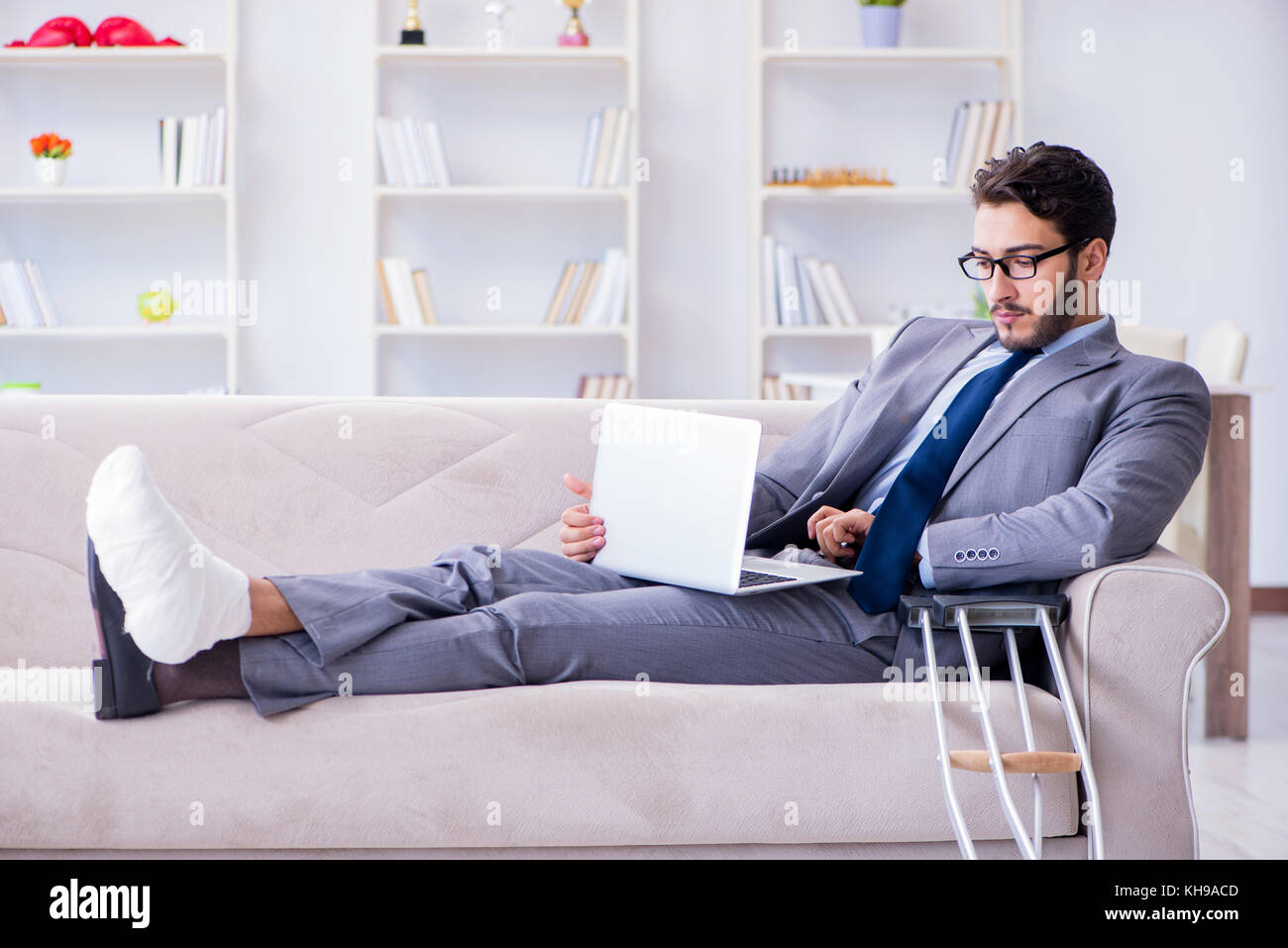 Businessman with crutches and broken leg at home working Stock Photo ...
