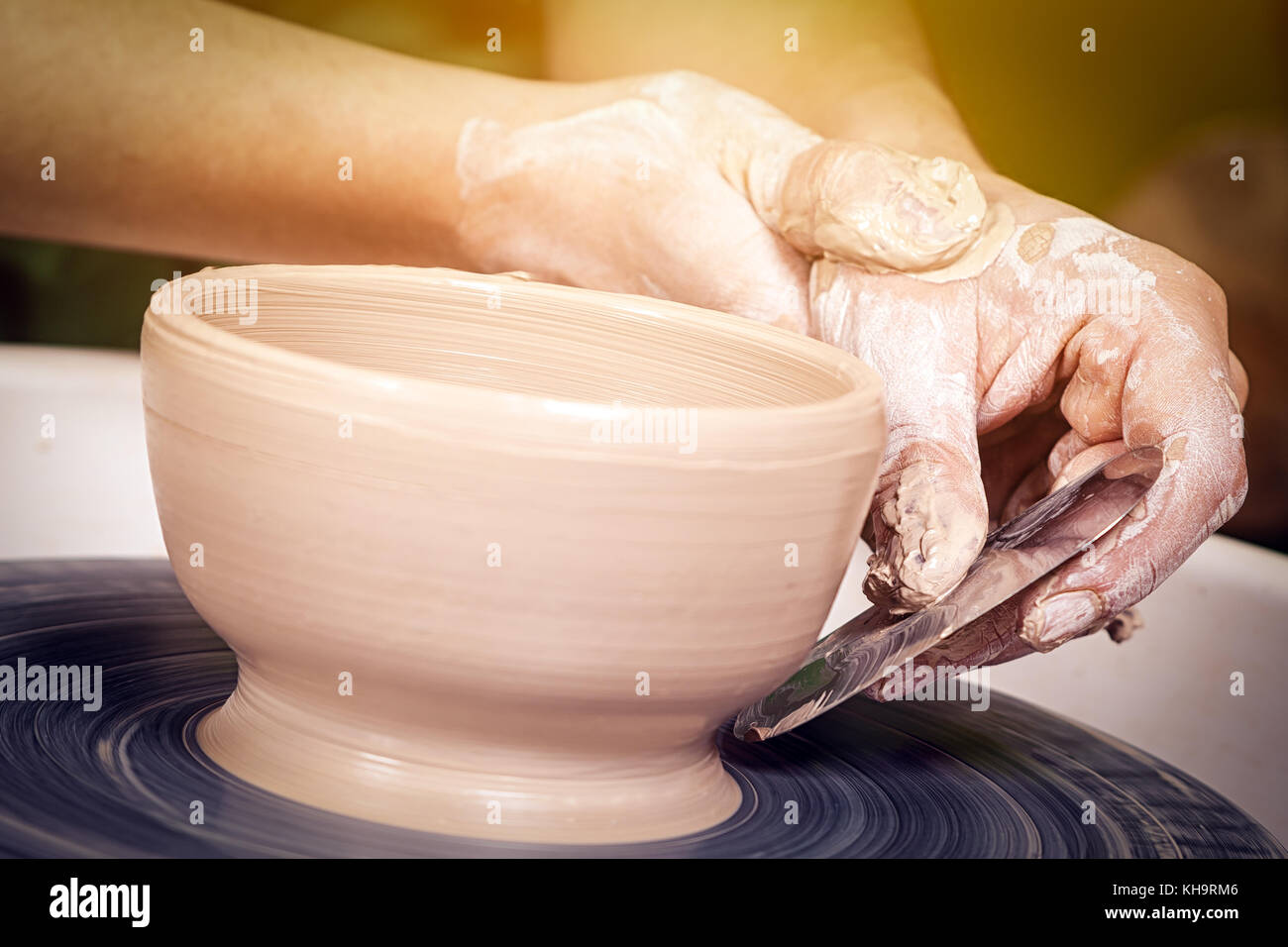 A close-up of a female potter sculpts a bowl of brown clay on a potter ...