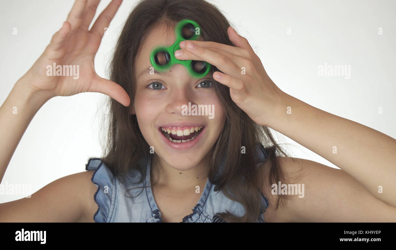 Beautiful cheerful teen girl playing with green fidget spinner on white ...
