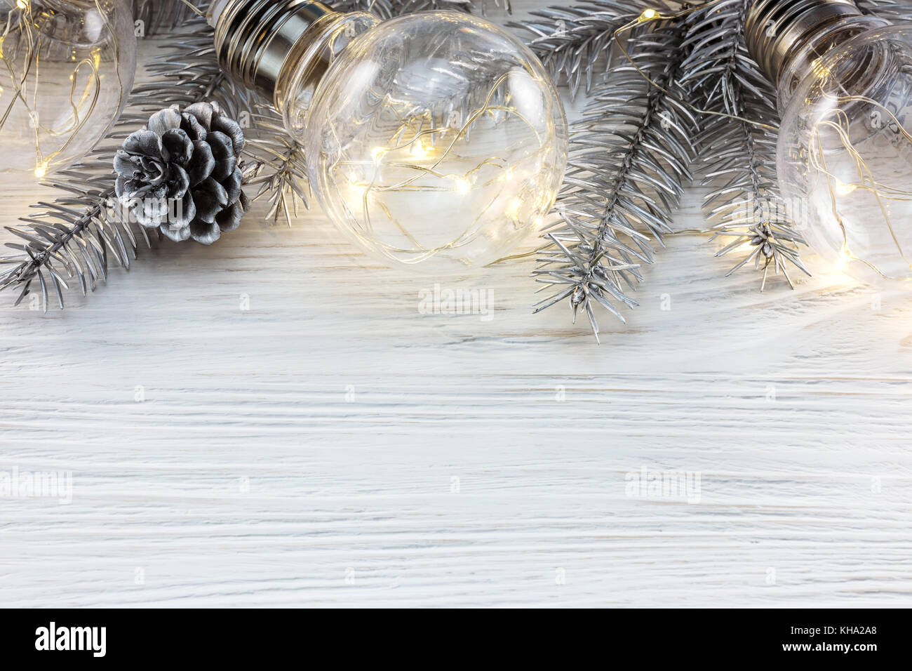 glowing decorative lamp bulbs and silver christmas tree branch on white ...
