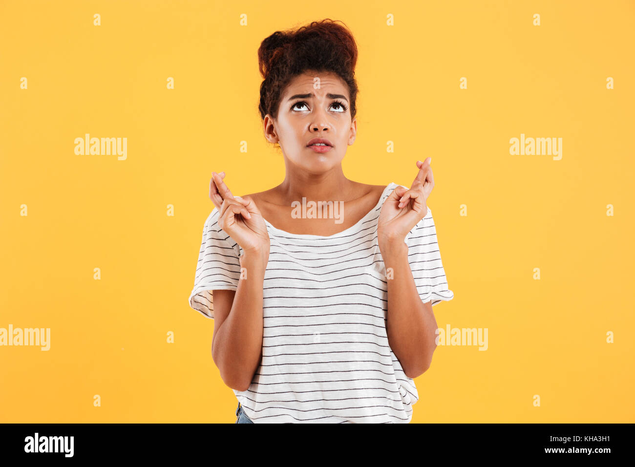 Young african nervous lady looking up and praying holding fingers ...
