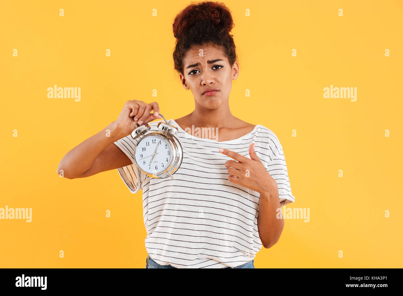 Upset african woman holding alarm clock and pointing on them over ...