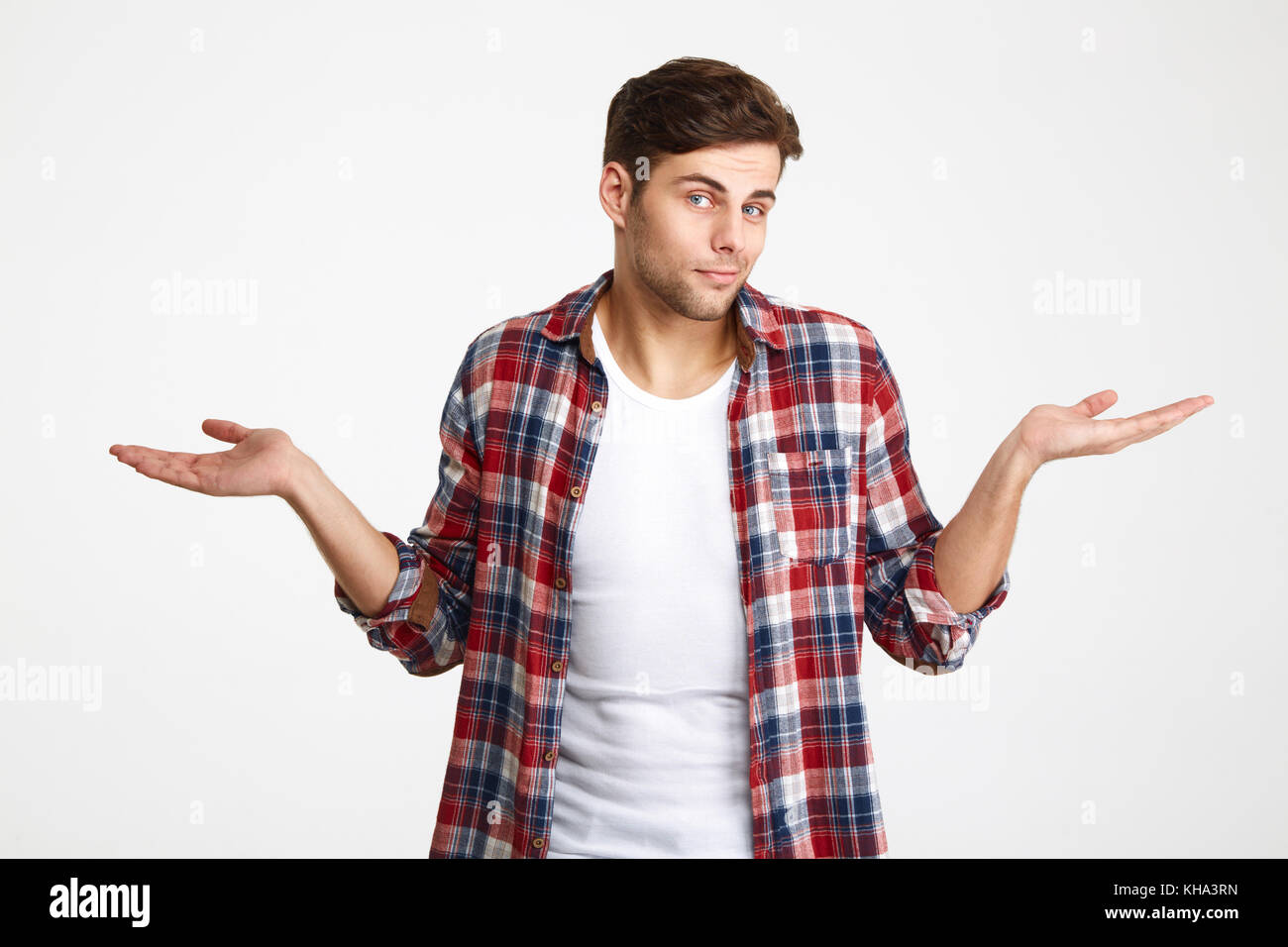 Portrait of a young doubtful man shrugging shoulders and looking at ...