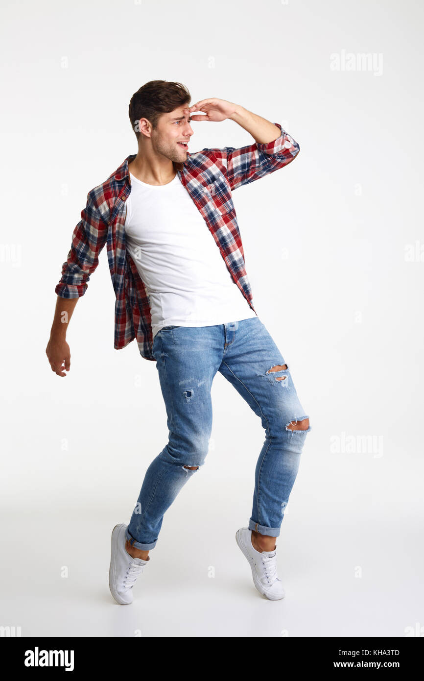 Full length portrait of a young casual man standing on his tiptoes and ...
