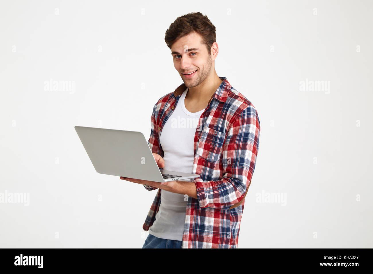 Portrait of a smiling young man holding laptop computer while standing ...