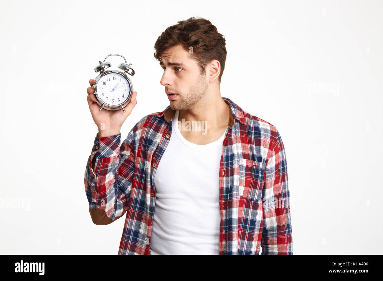 Portrait of a restless man holding and looking at alarm clock isolated ...