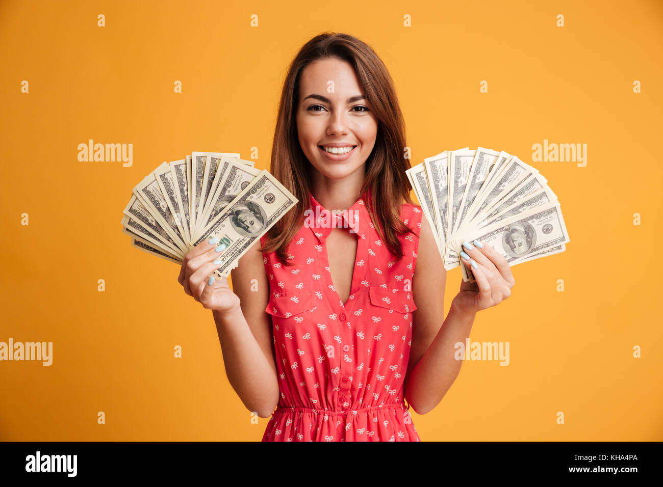 Young cheerful woman holding two fans of money, looking at camera ...