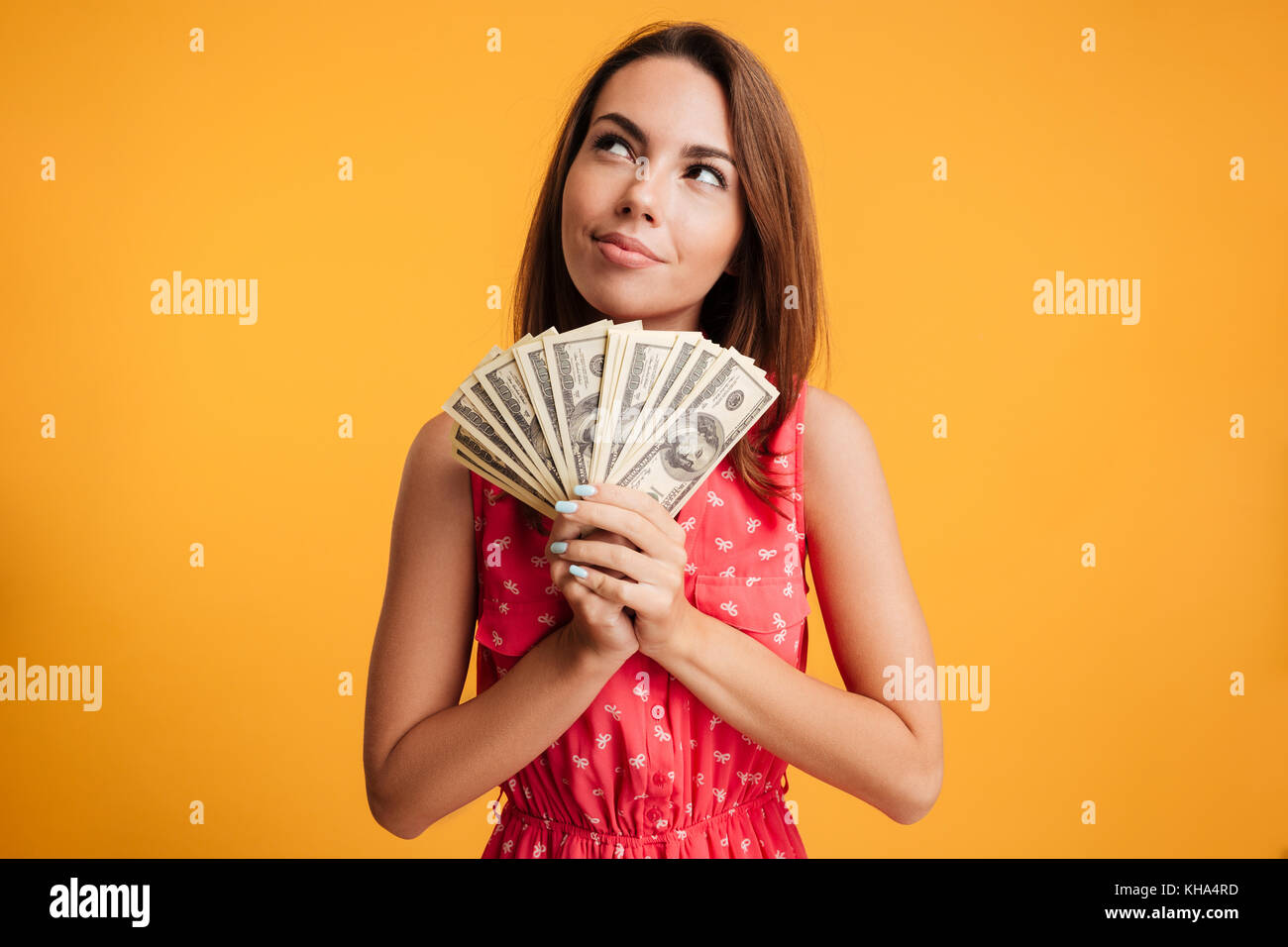 Young attractive smiling woman thinking how to spend her bunch of money ...
