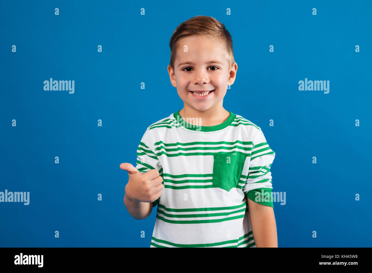 Portrait of a happy kid showing thumbs up gesture isolated over blue ...