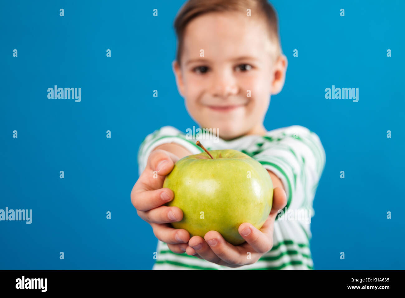 Image of Smiling young boy giving apple at the camera over blue ...