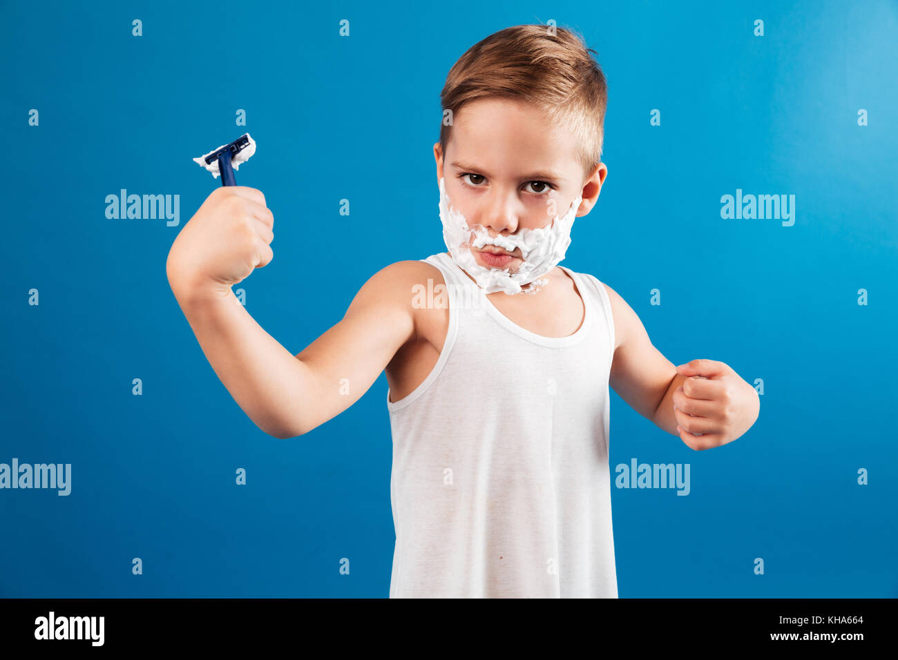 Serious young boy in shaving foam like man holding razor and showing ...
