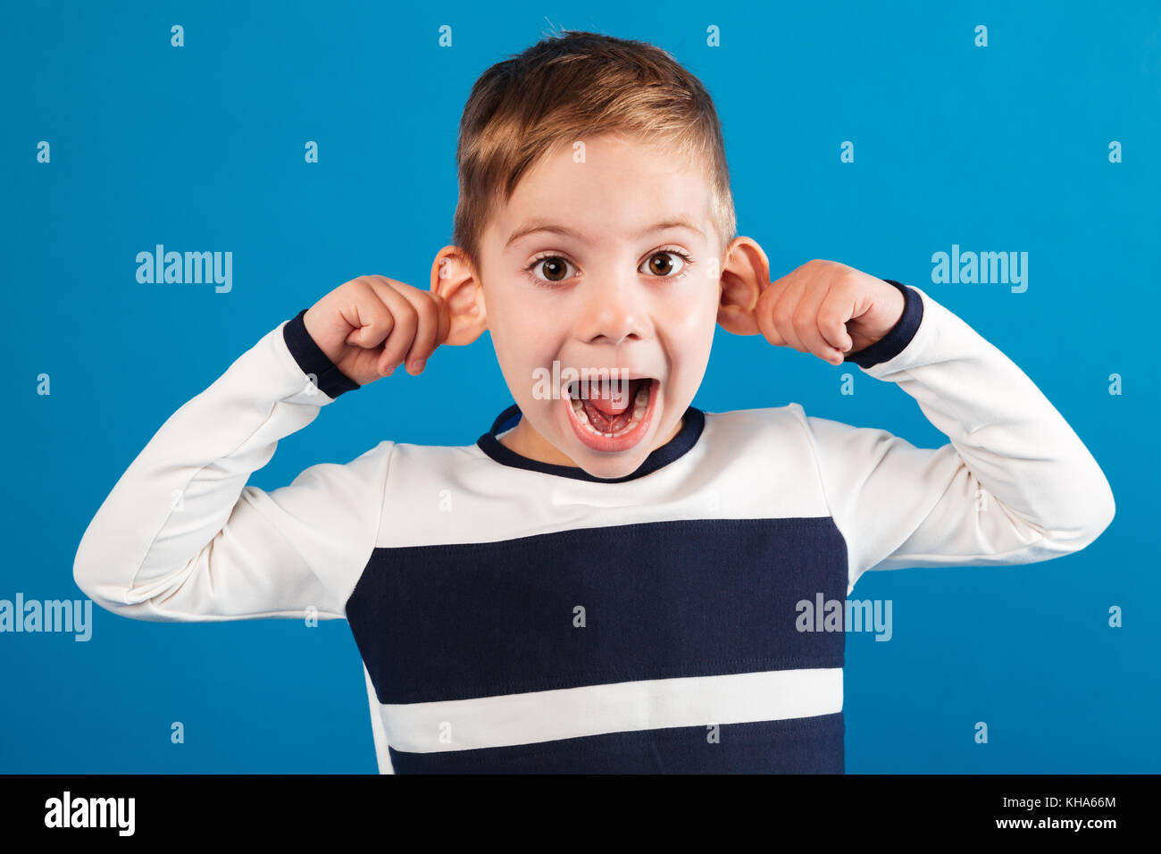 Funny happy young boy in sweater showing grimace at camera over blue ...