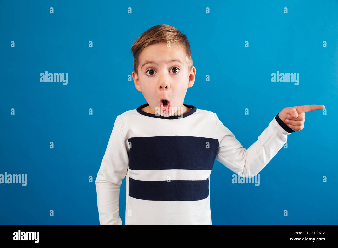 Shocked young boy in sweater pointing away and looking at the camera ...