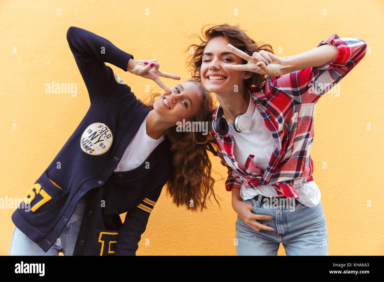Two happy cheerful teenage girls showing peace gesture while having fun ...