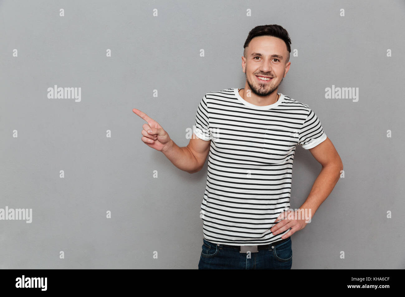 Portrait of a casual young man pointing finger away at copy space and ...