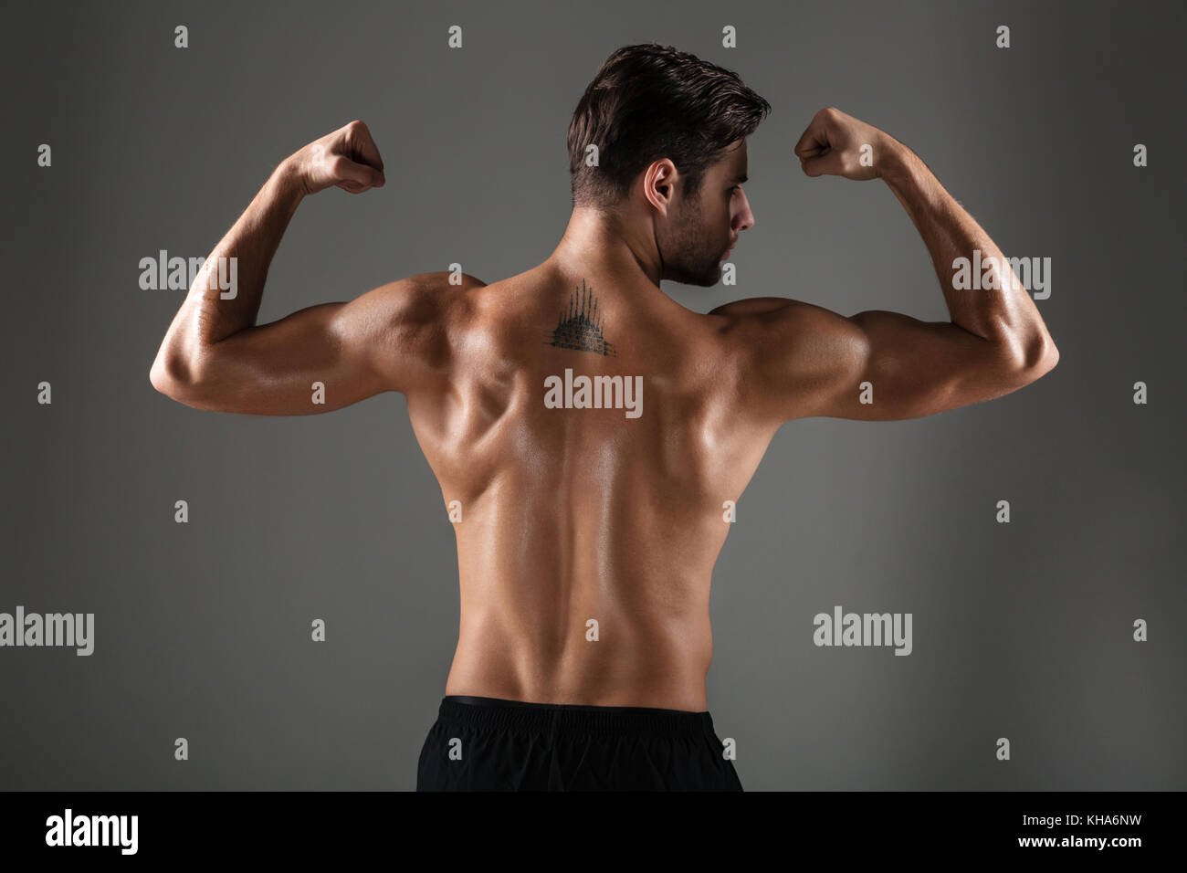 Back view image of young sports man showing biceps isolated over grey ...