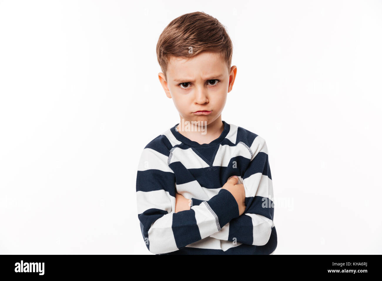 Portrait of an upset cute little kid standing with arms folded and ...