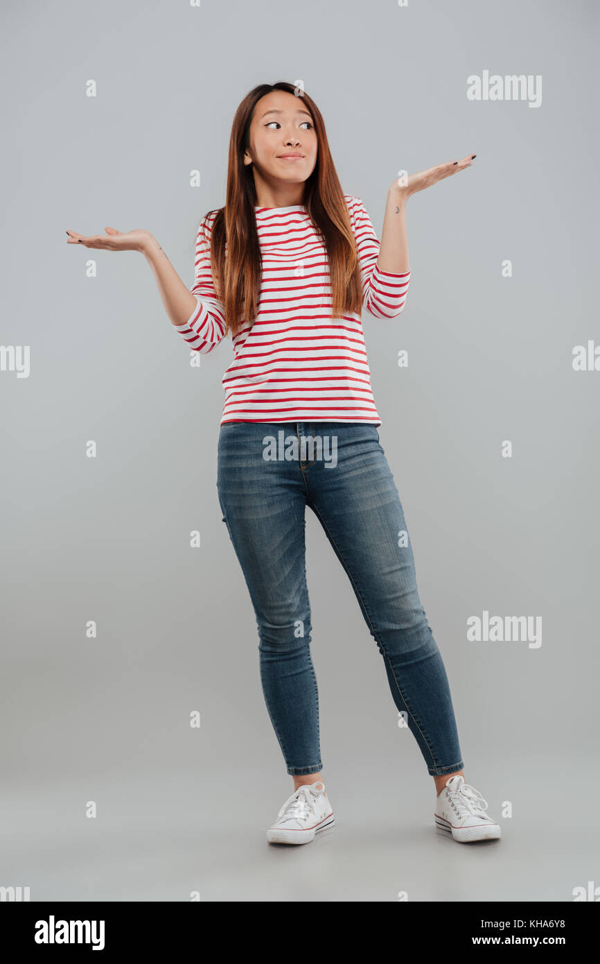 Full length portrait of a confused funny girl shrugging her shoulders ...