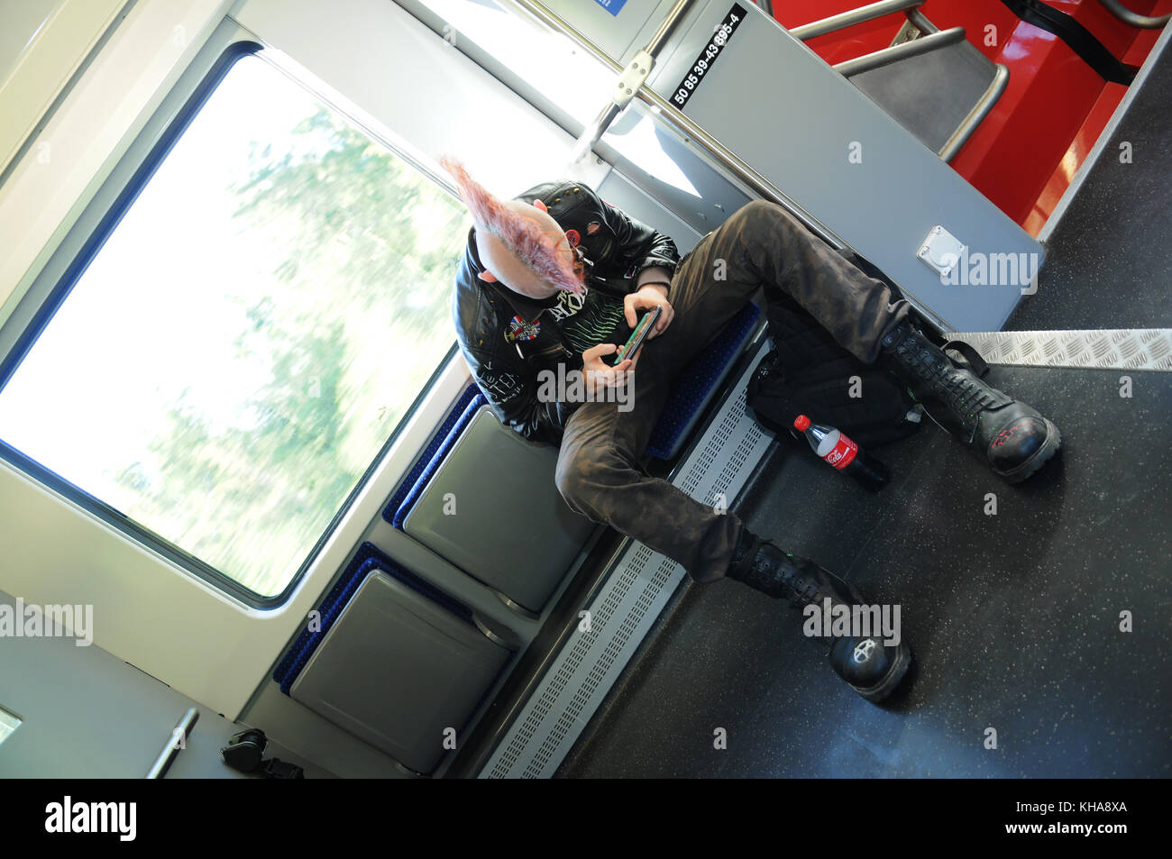 Switzerland, punk with pink hair staring at his smartphone in the train ...