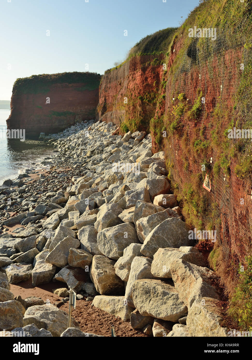 Rock armour - large boulders piled against red sandstone cliffs to ...