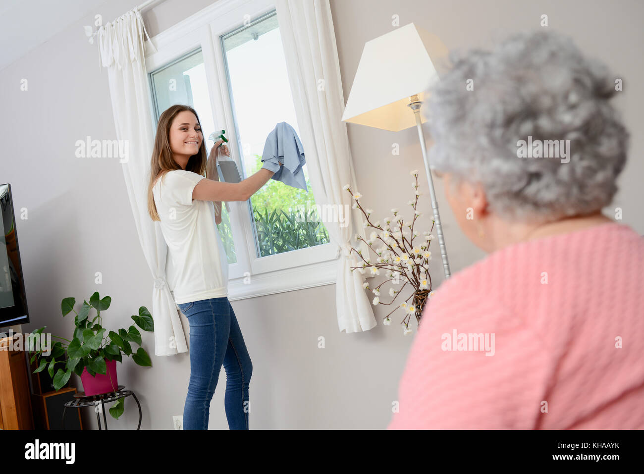 Cheerful young girl helping with household chores elderly woman at home ...