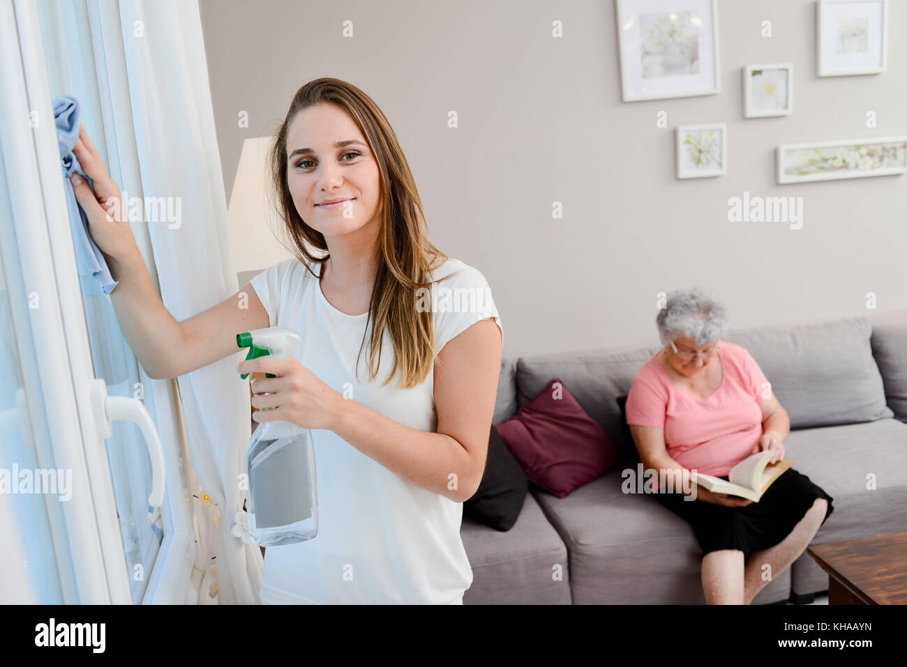 Cheerful young girl helping with household chores elderly woman at home ...