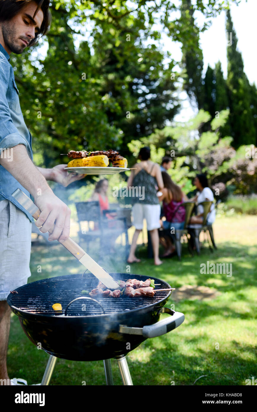 Handsome young man cooking meat in a barbecue party outdoor in the ...