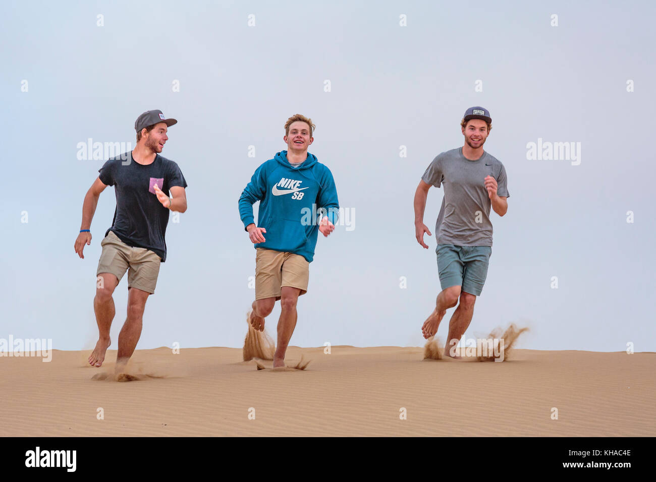 Three young men running down sand dune, Namib Desert, Namibia Stock ...