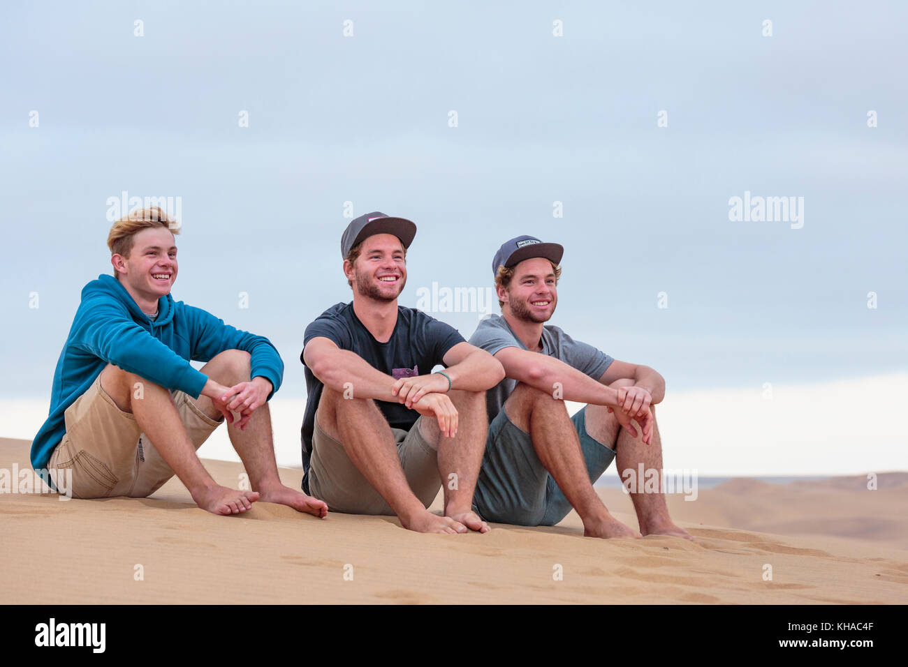 Three young men sitting on sand dune, Namib Desert, Namibia Stock Photo ...