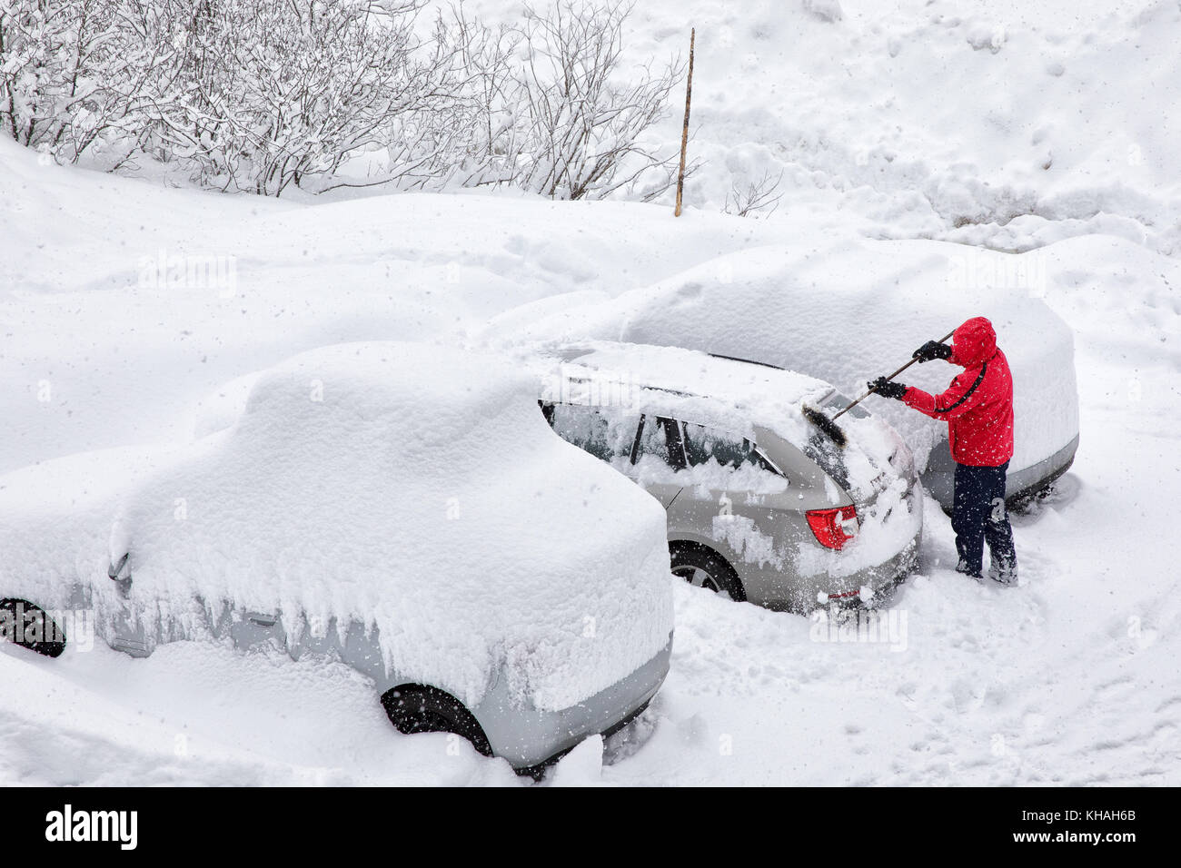 Young attractive man brushing the snow off his car on a cold winter day ...