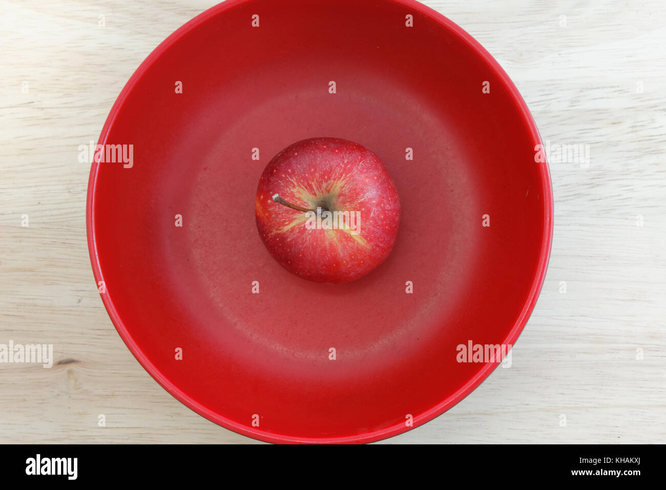 Red apple inside a red bowl on wooden table Stock Photo - Alamy