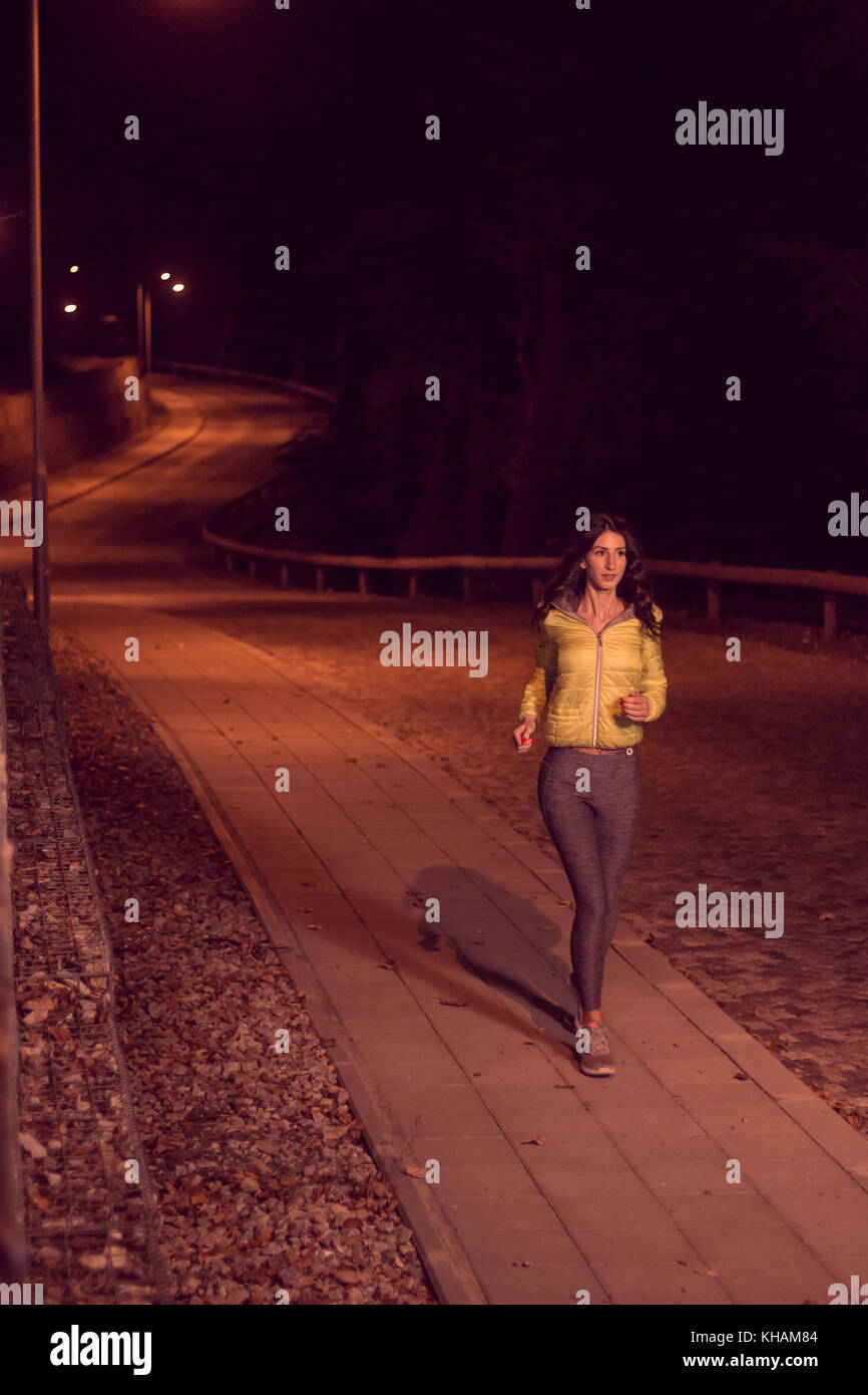 one young woman, alone one person, jogging sidewalk, outdoors night ...